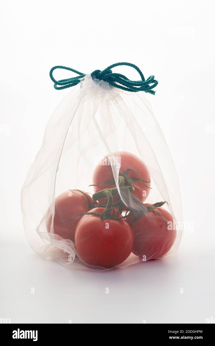 Still life with tomatoes in net mesh bag back lit on white background ...
