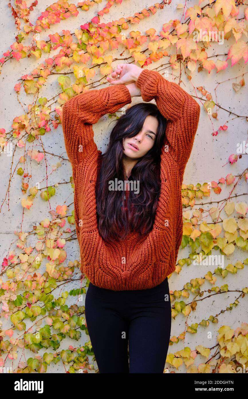 Pensive young long haired brunette in warm knitted sweater standing ...