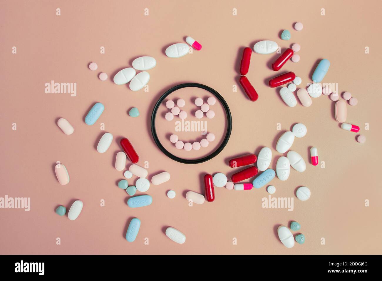 Smiley face made up of pills on a pastel orange table with some other ...