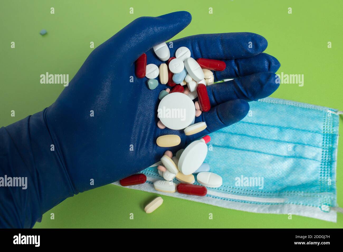 A gloved hand drops some medications onto a surgical mask on a green ...