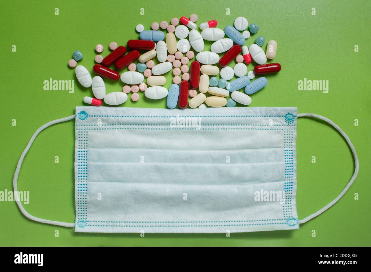 A face mask and a pile of pills and capsules on a green background ...