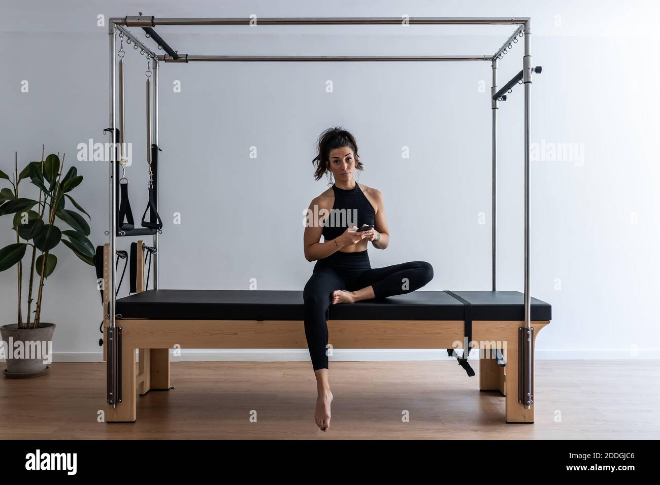 Fit female athlete sitting on pilates cadillac reformer and browsing ...