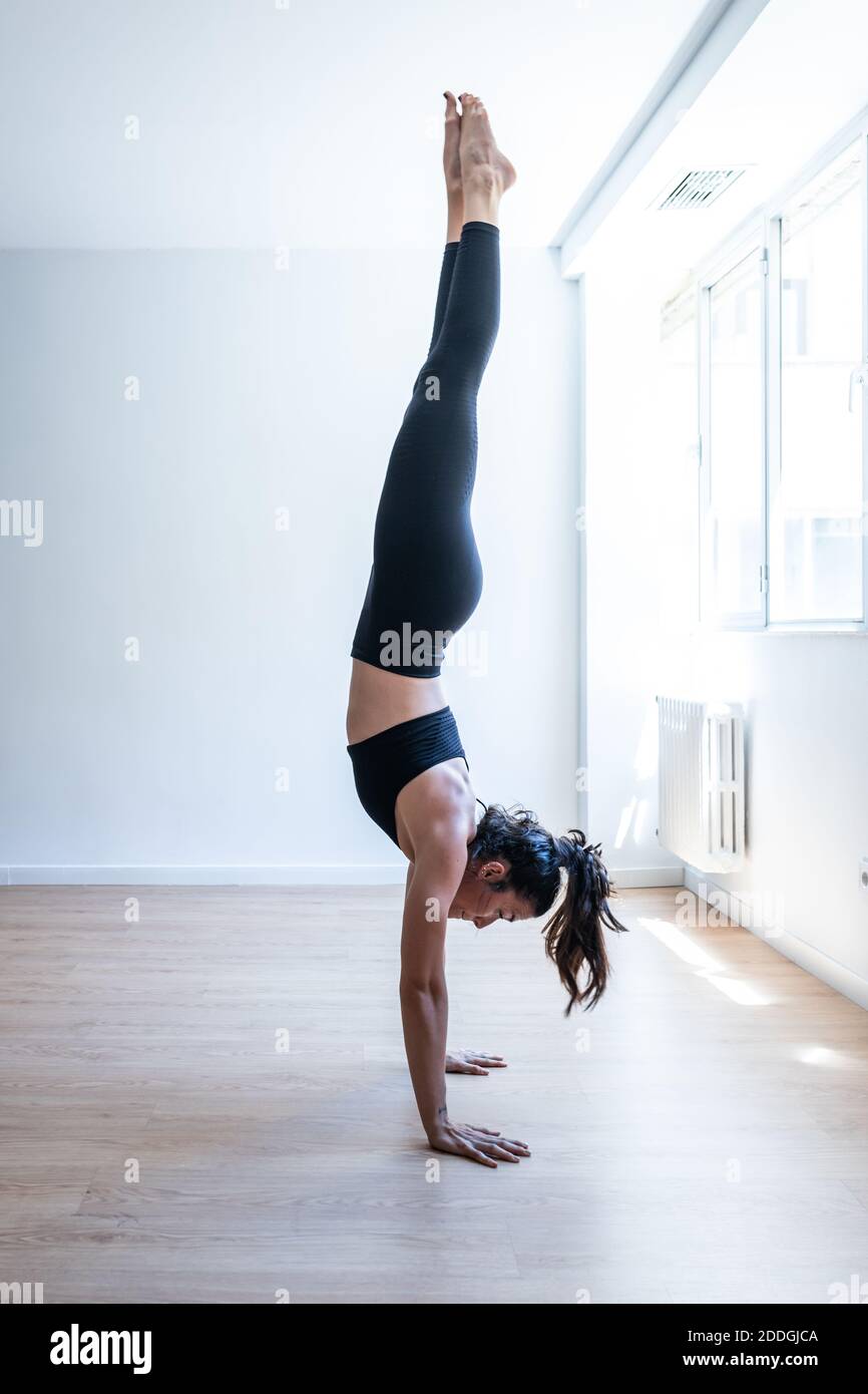 Side view of slim female athlete performing handstand on wooden floor ...