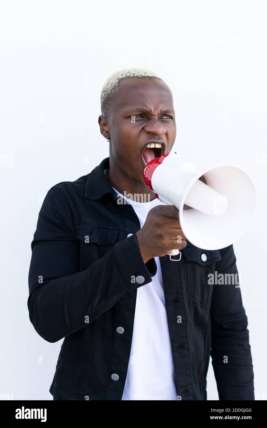 African American male shouting in loudspeaker while standing on white ...