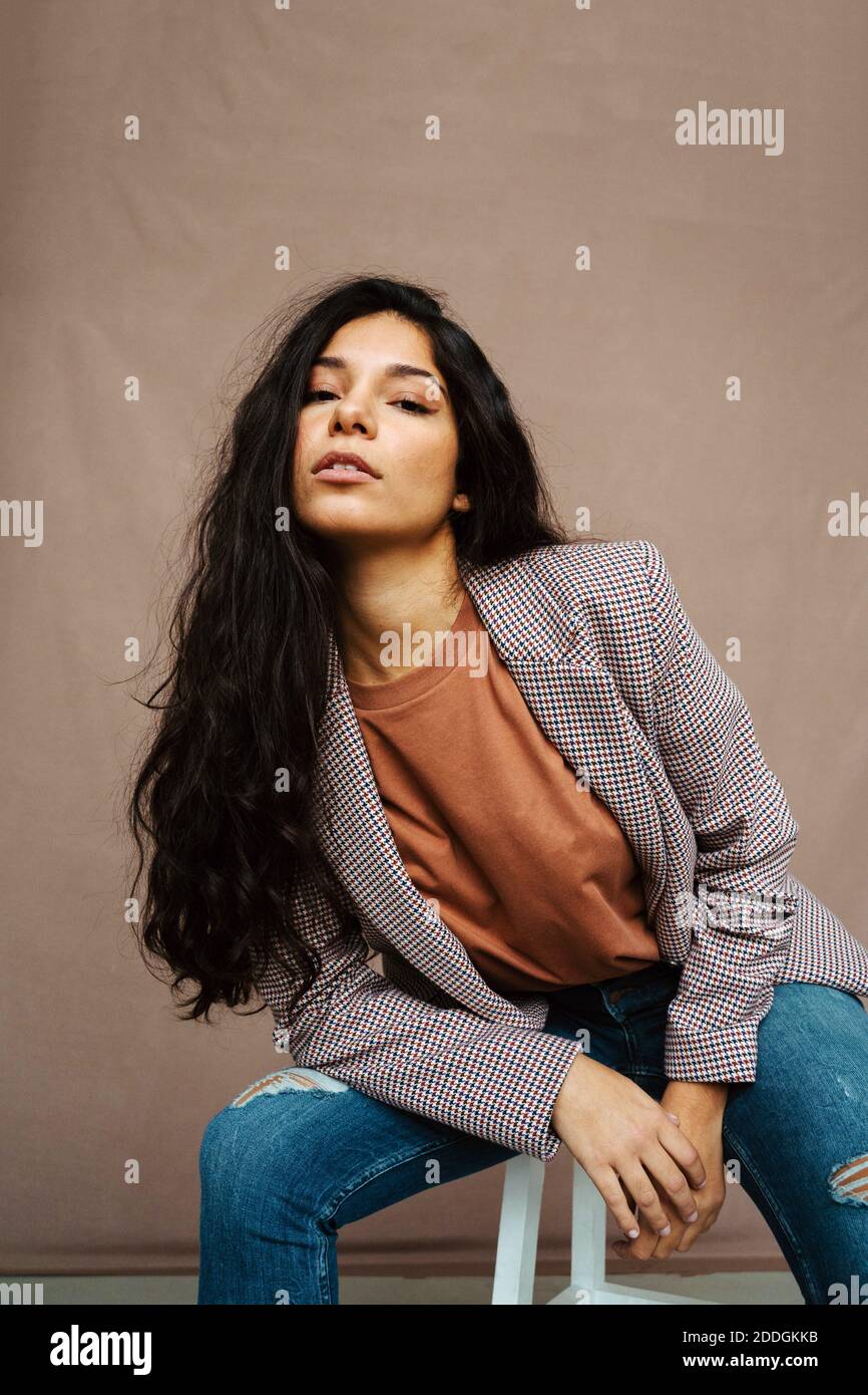 Stylish ethnic female model in trendy smart casual outfit sitting on ...