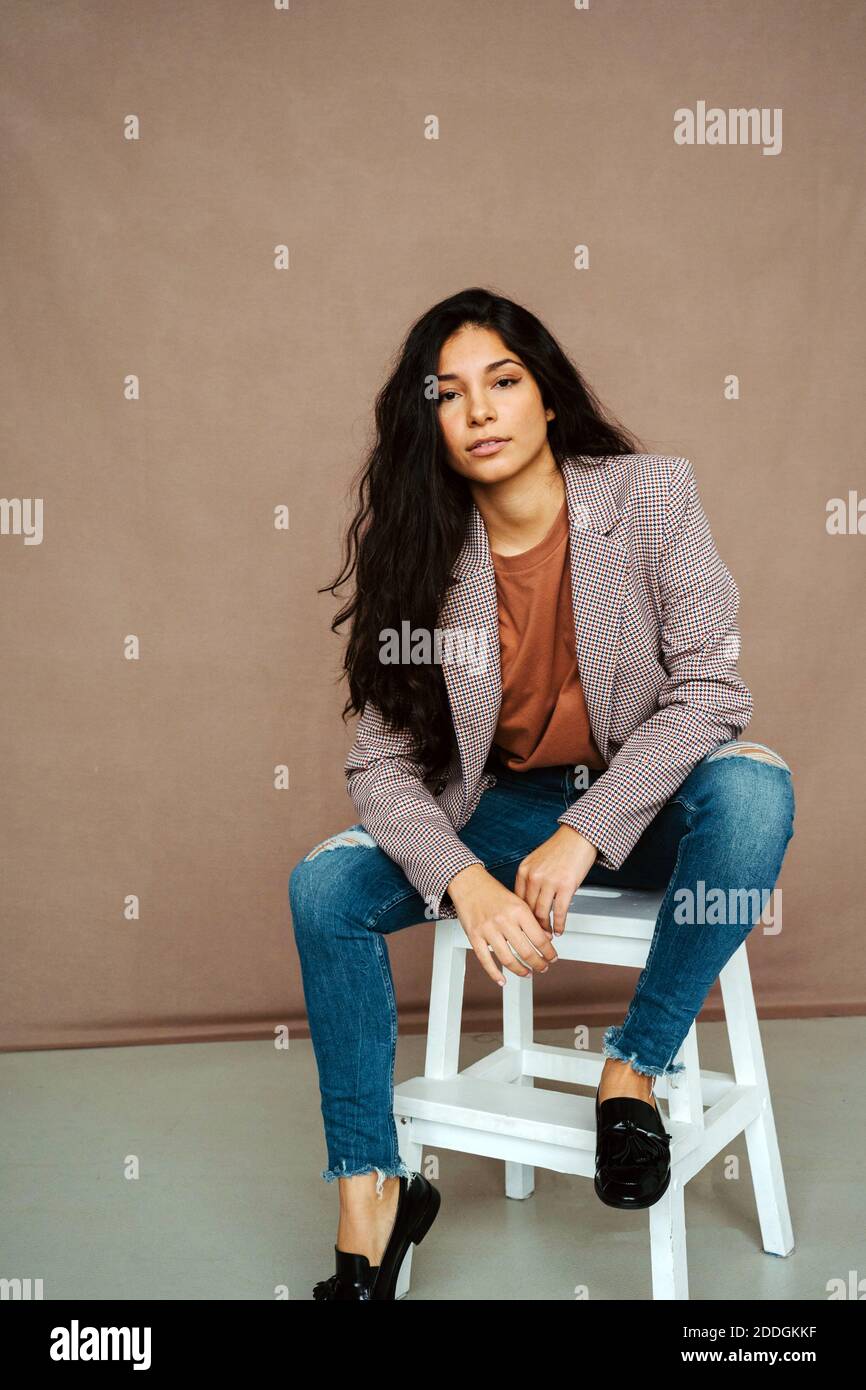 Stylish ethnic female model in trendy smart casual outfit sitting on ...