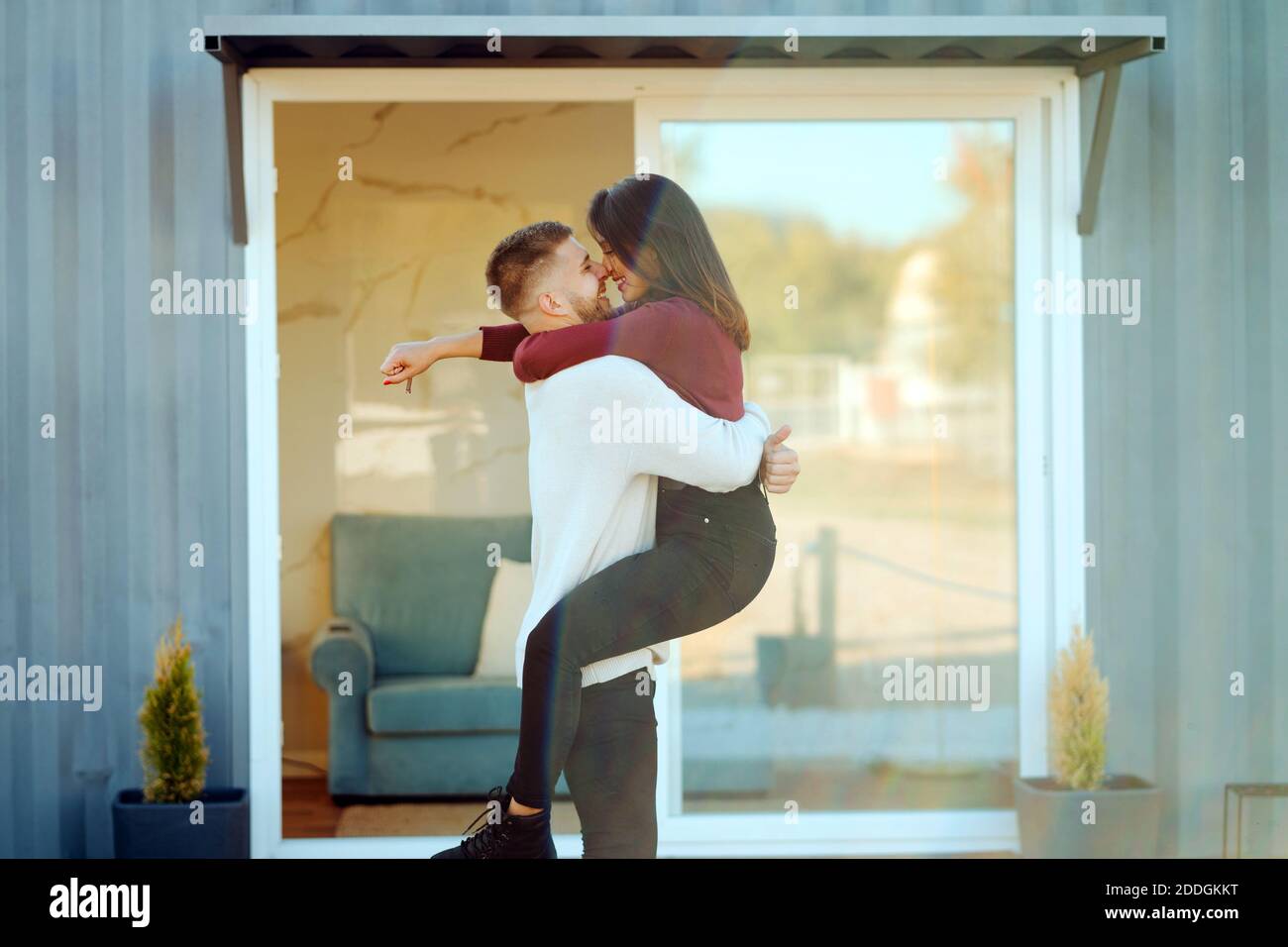 Side view of cheerful couple cuddling and kissing near new container ...