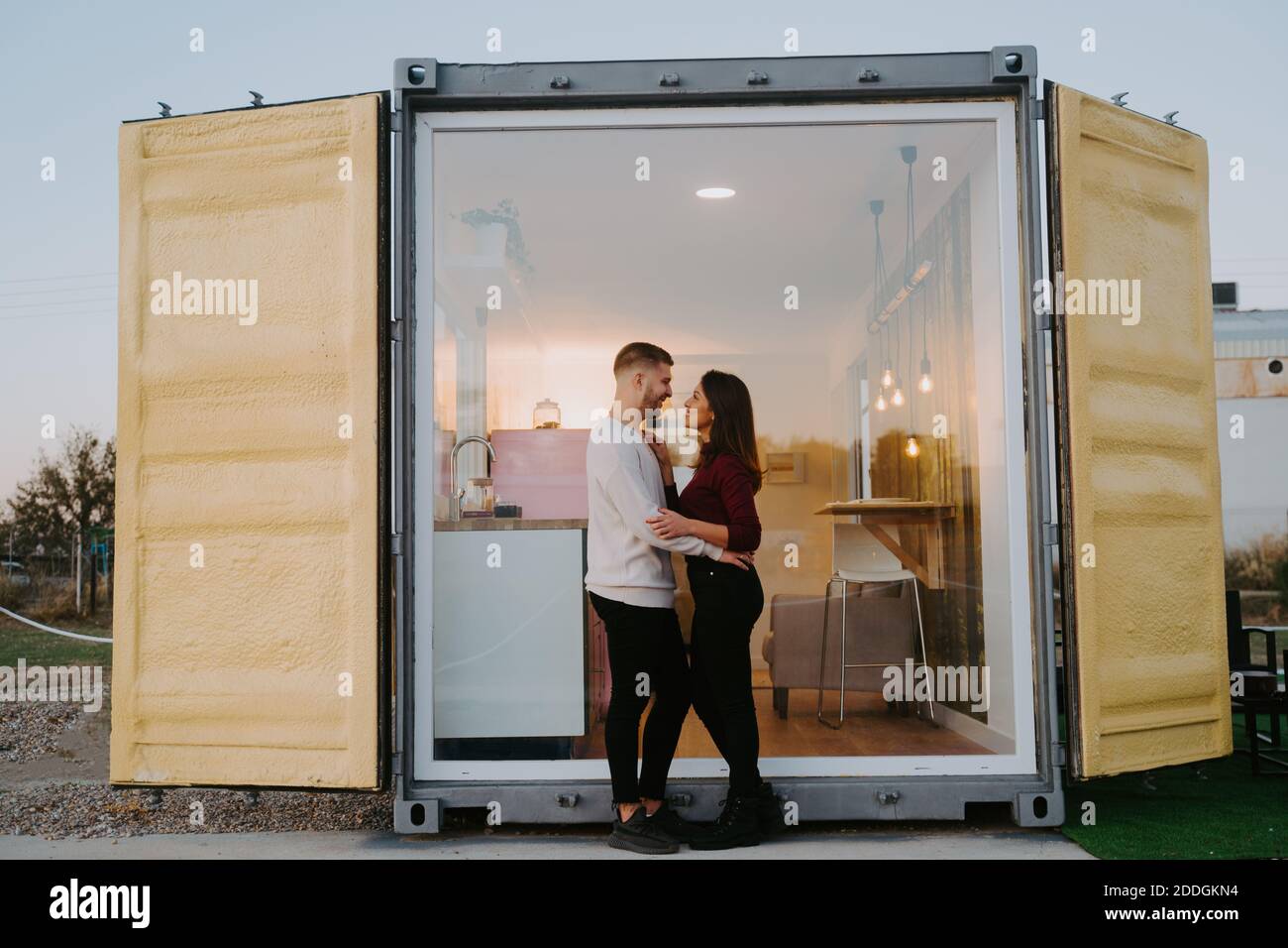 Side view of smiling couple cuddling near window of modern container ...
