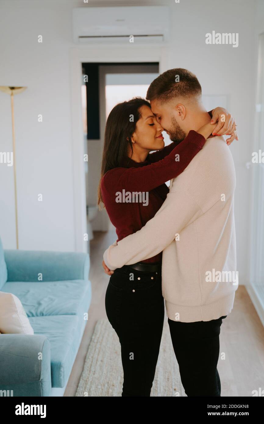 Side view of couple in love standing in living room and cuddling while ...