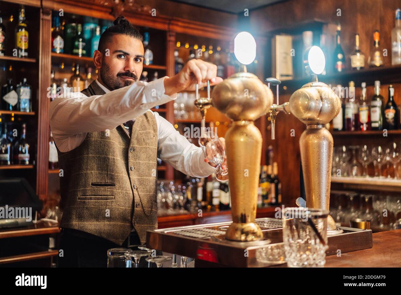 Concentrated adult bearded bartender tapping beer into glass while ...