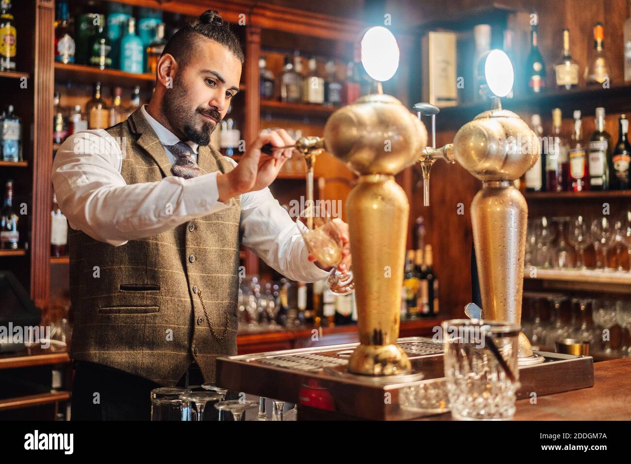 Concentrated adult bearded bartender tapping beer into glass while ...