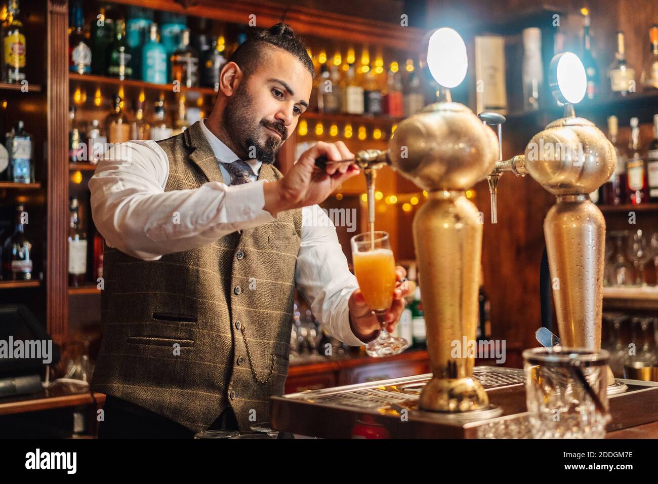 Concentrated adult bearded bartender tapping beer into glass while ...