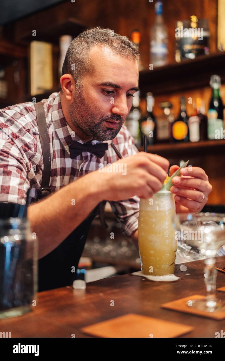 Middle aged man in apron and checkered shirt decorating glass of ...