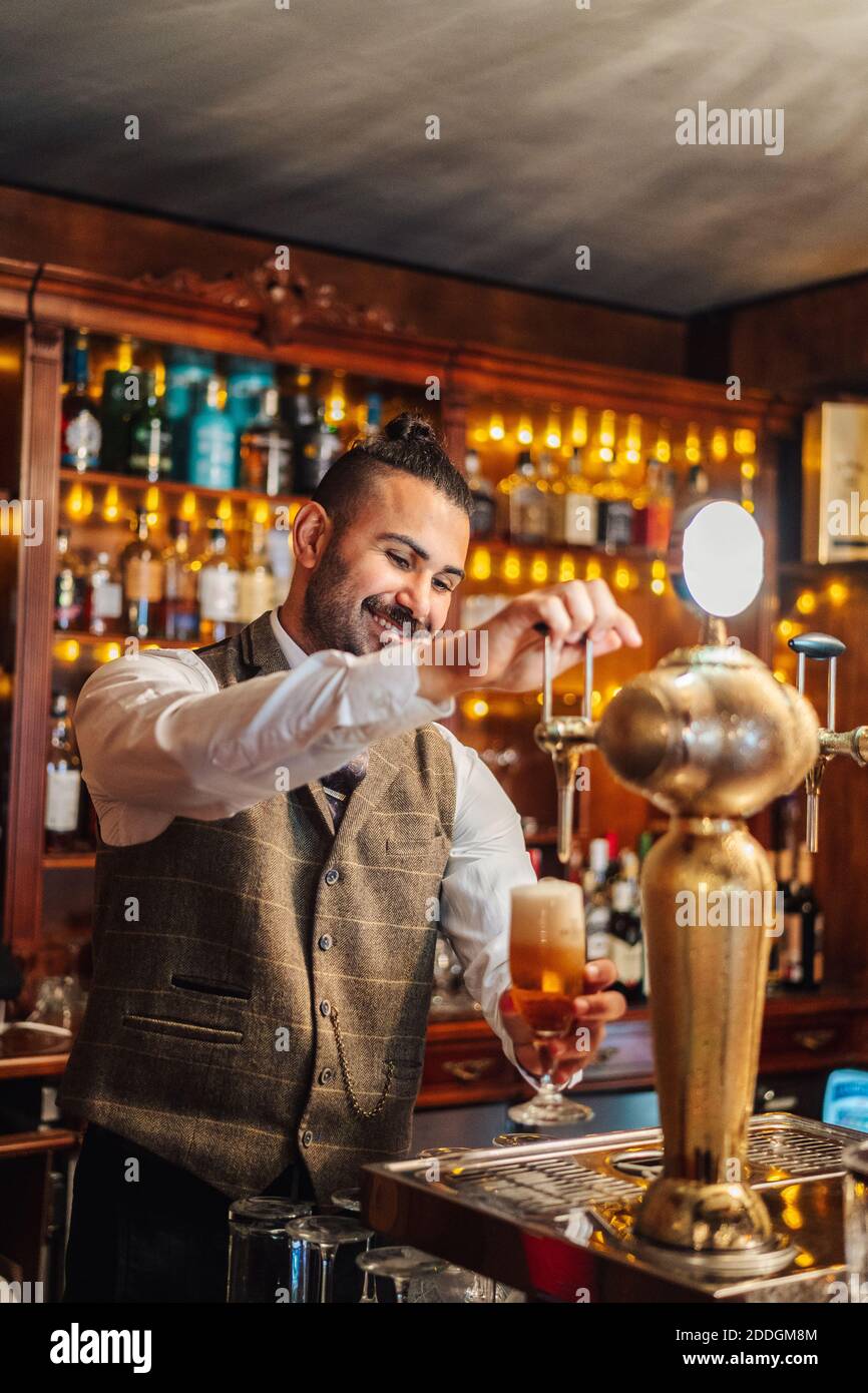 Concentrated adult bearded bartender tapping beer into glass while ...