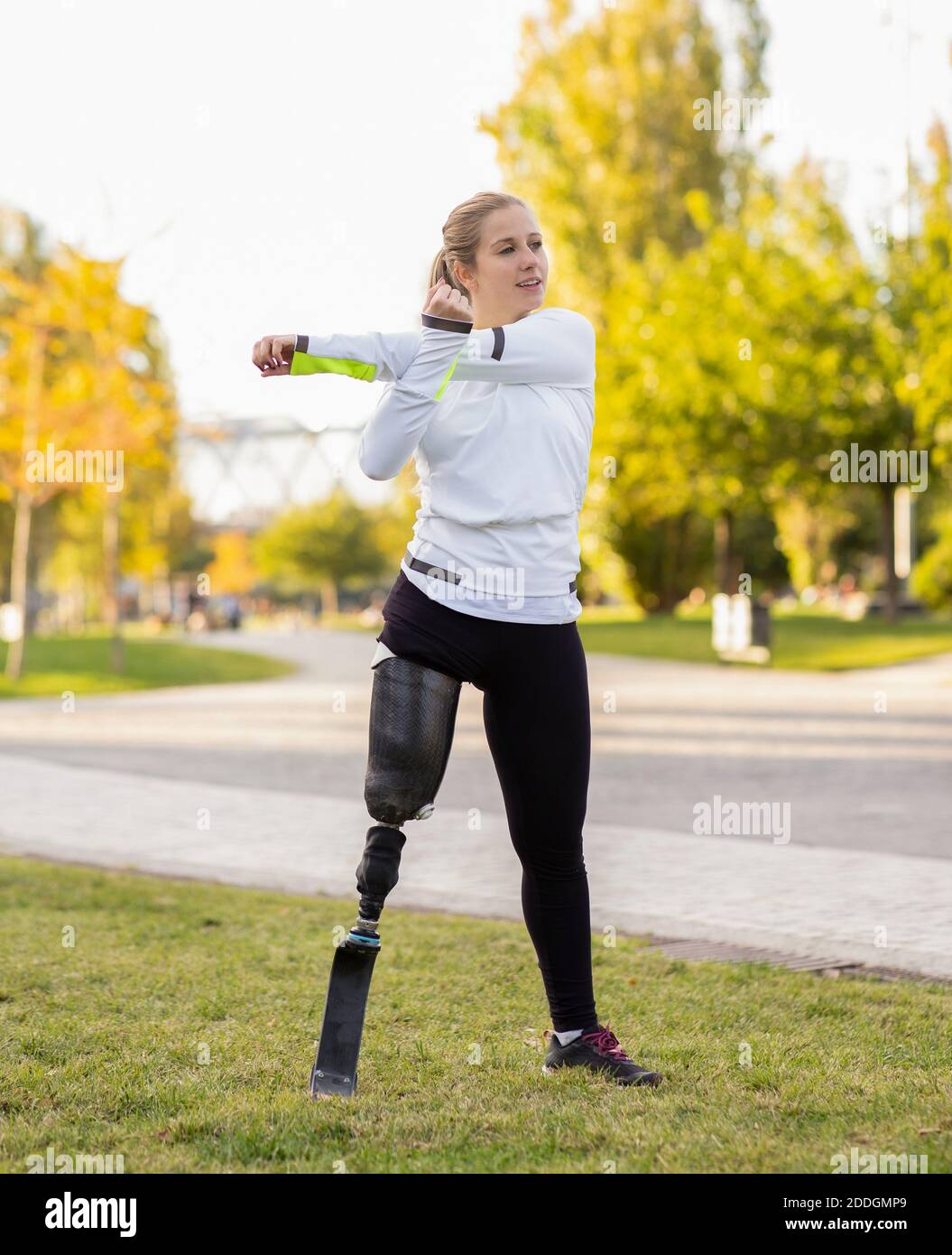 Focused Paralympic female runner with leg prosthesis stretching body ...