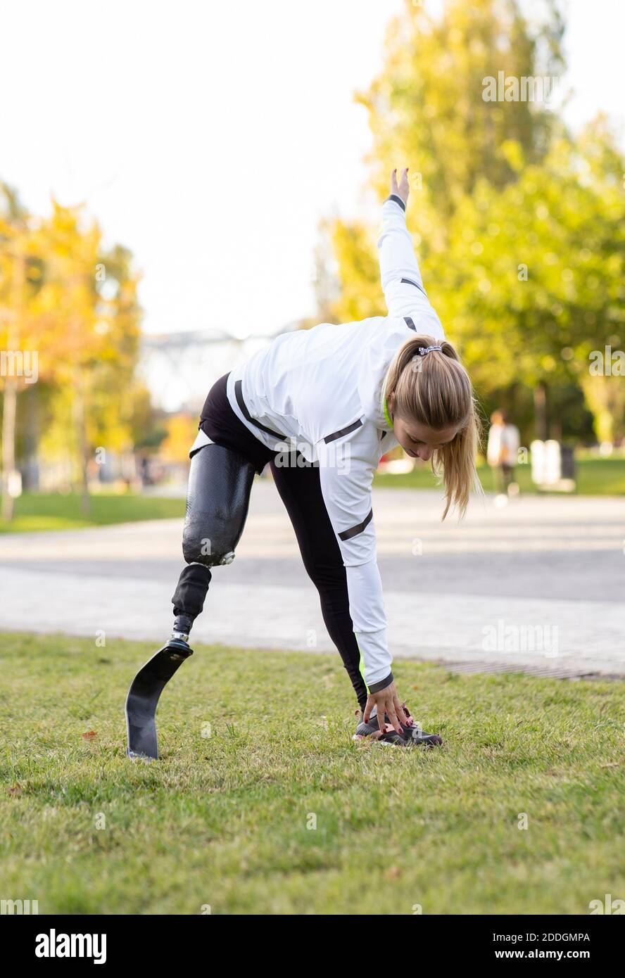 Focused Paralympic female runner with leg prosthesis stretching body ...