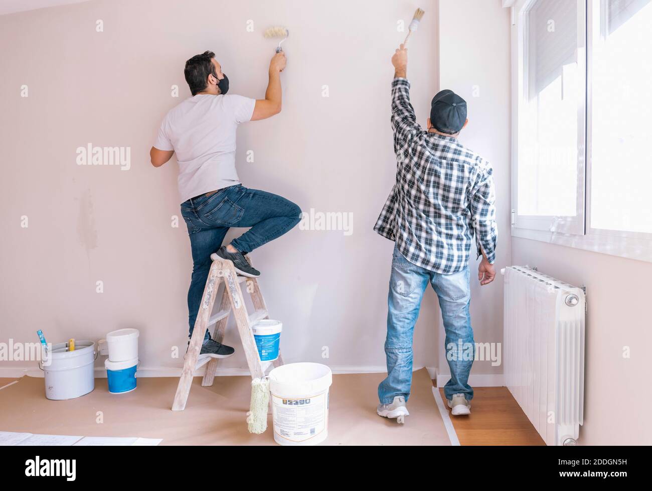 Back view of male painters covering wall with bright paint while ...