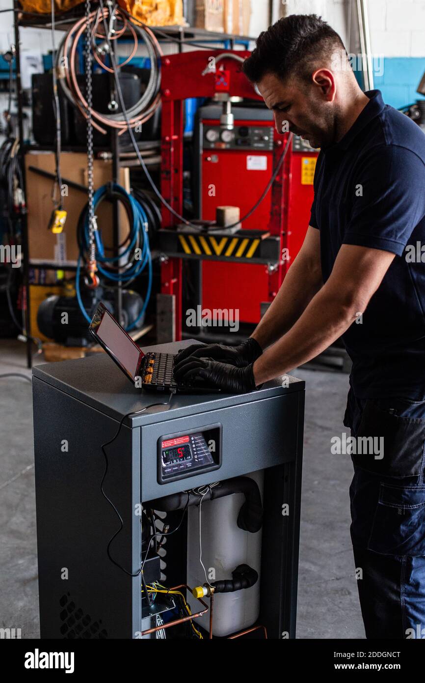 Adult man in using laptop to program broken machine during work in ...