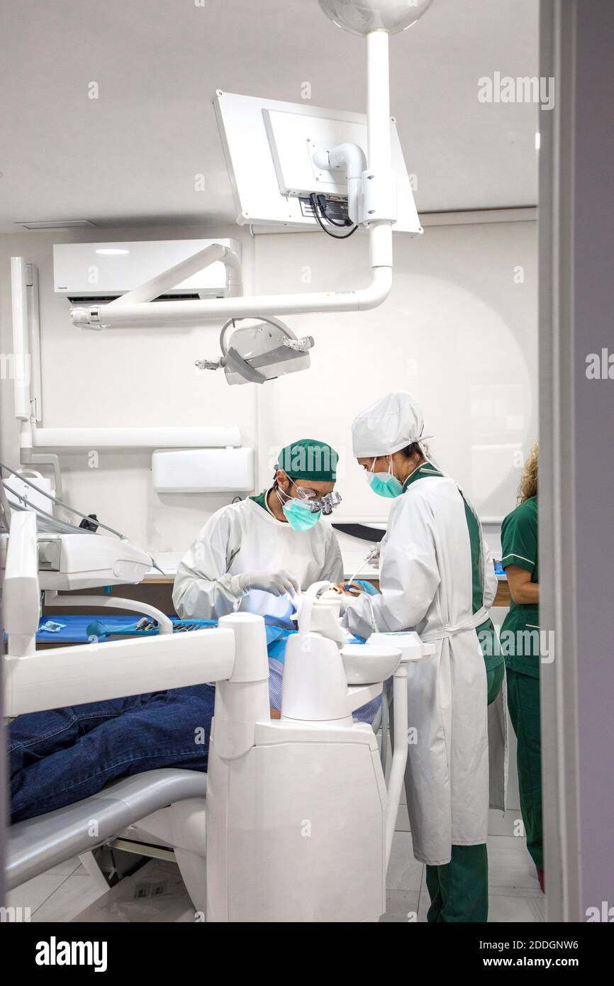 Dentists in masks and uniform operating patient lying in dental chair ...