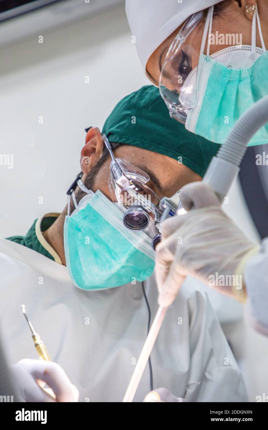 Dentists in masks and uniform operating patient lying in dental chair ...