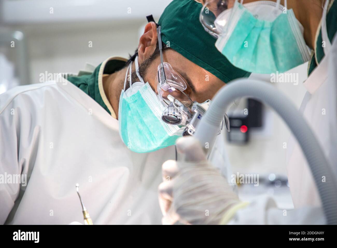 Dentists in masks and uniform operating patient lying in dental chair ...