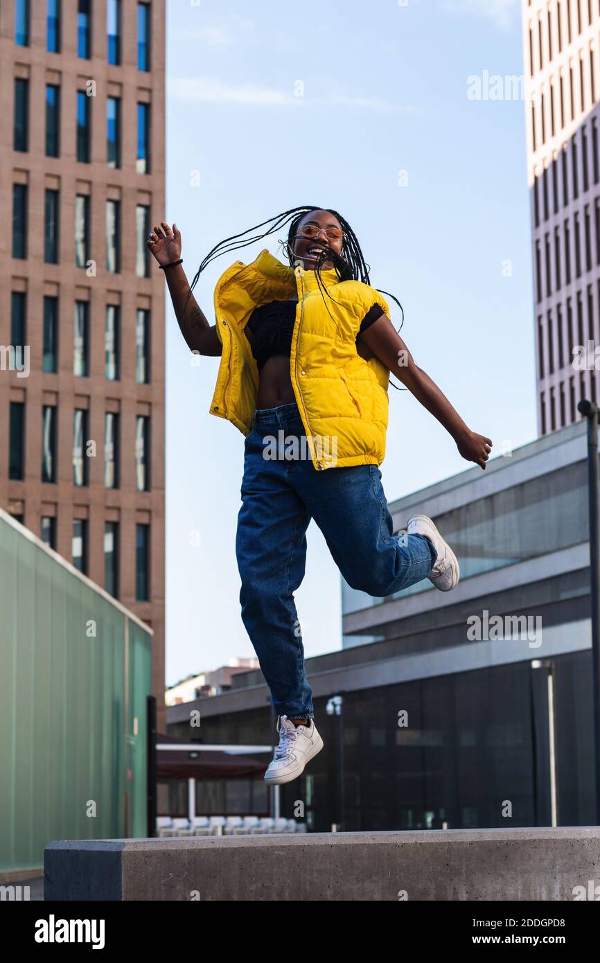 Happy black Woman in trendy clothes laughing and leaping up on street ...