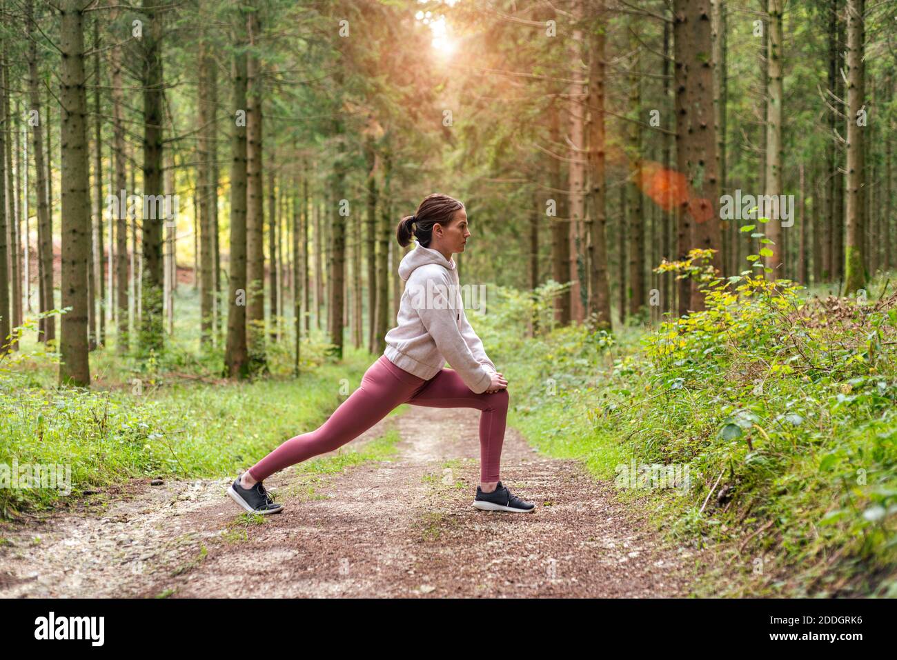Side view of female runner warming up legs and doing lunges while ...
