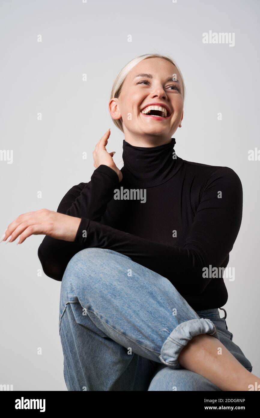 Cheerful blonde female in casual apparel sitting in studio and laughing ...