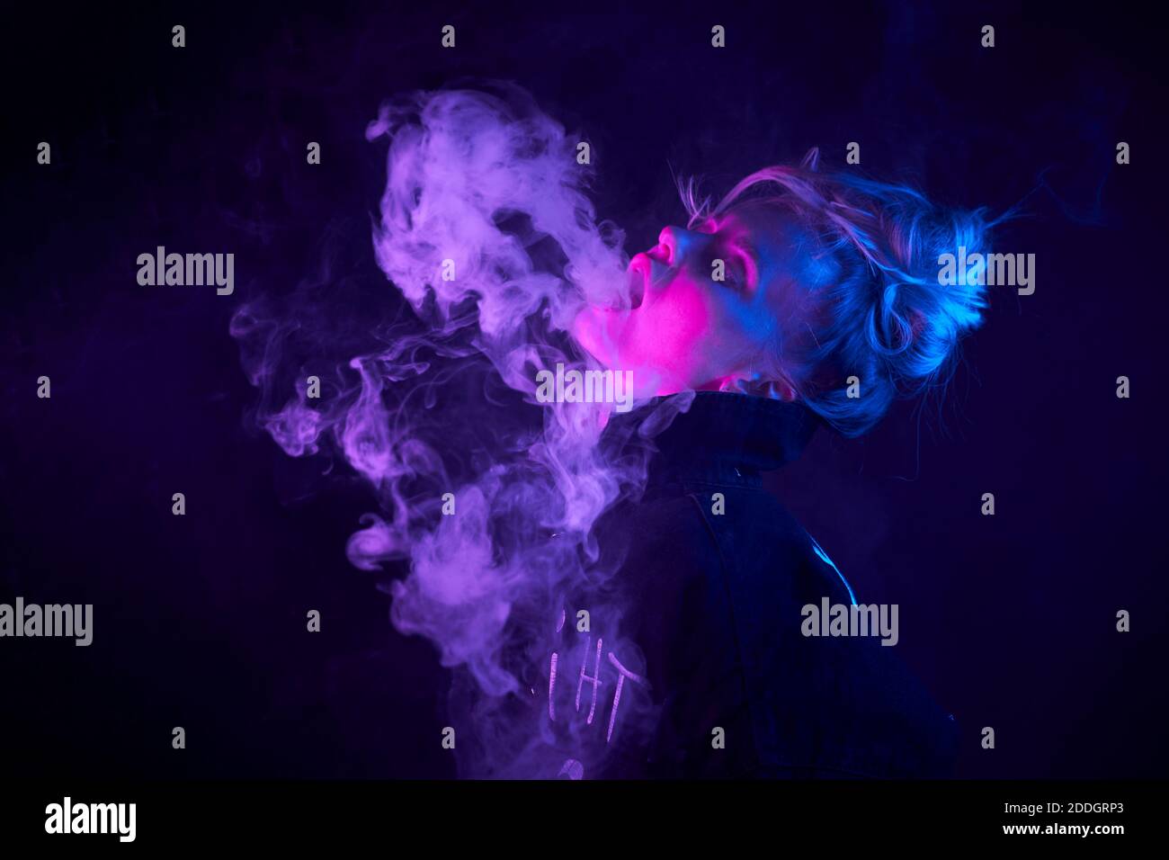 Side view of young cool female smoking vape in neon light in dark ...
