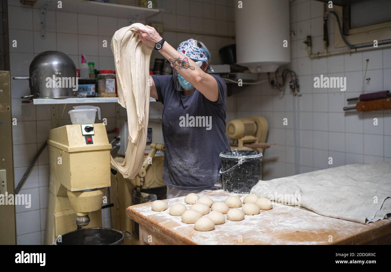Unrecognizable female baker in mask working in bakery and kneading raw ...