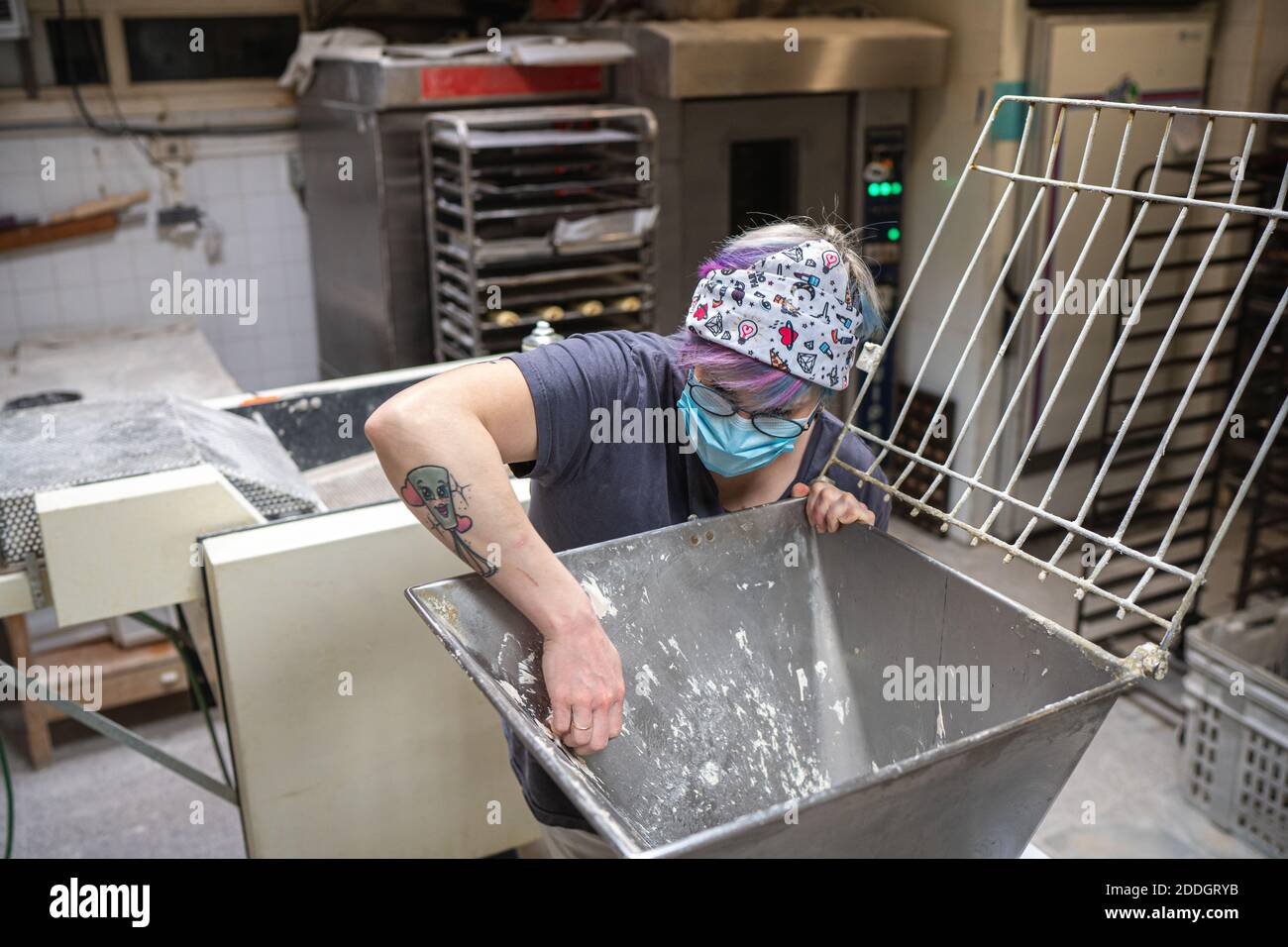 Female baker in protective mask cleaning metal baking machine from ...