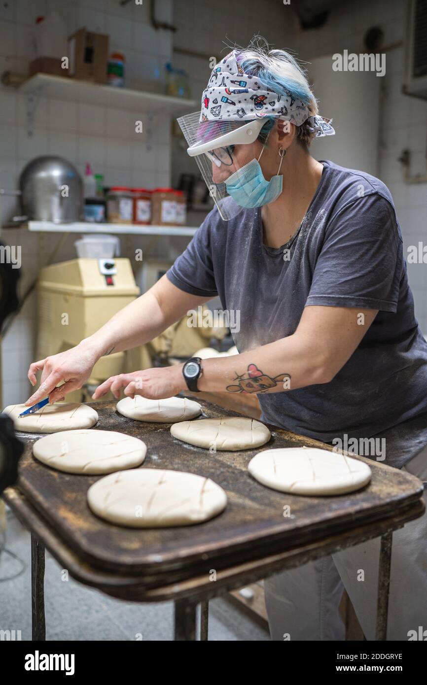 Female baker wearing mask and shield standing at table and making ...