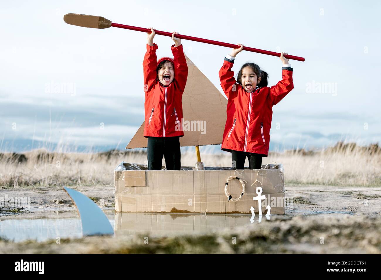 Optimistic children standing in carton boat with paddle above heads ...