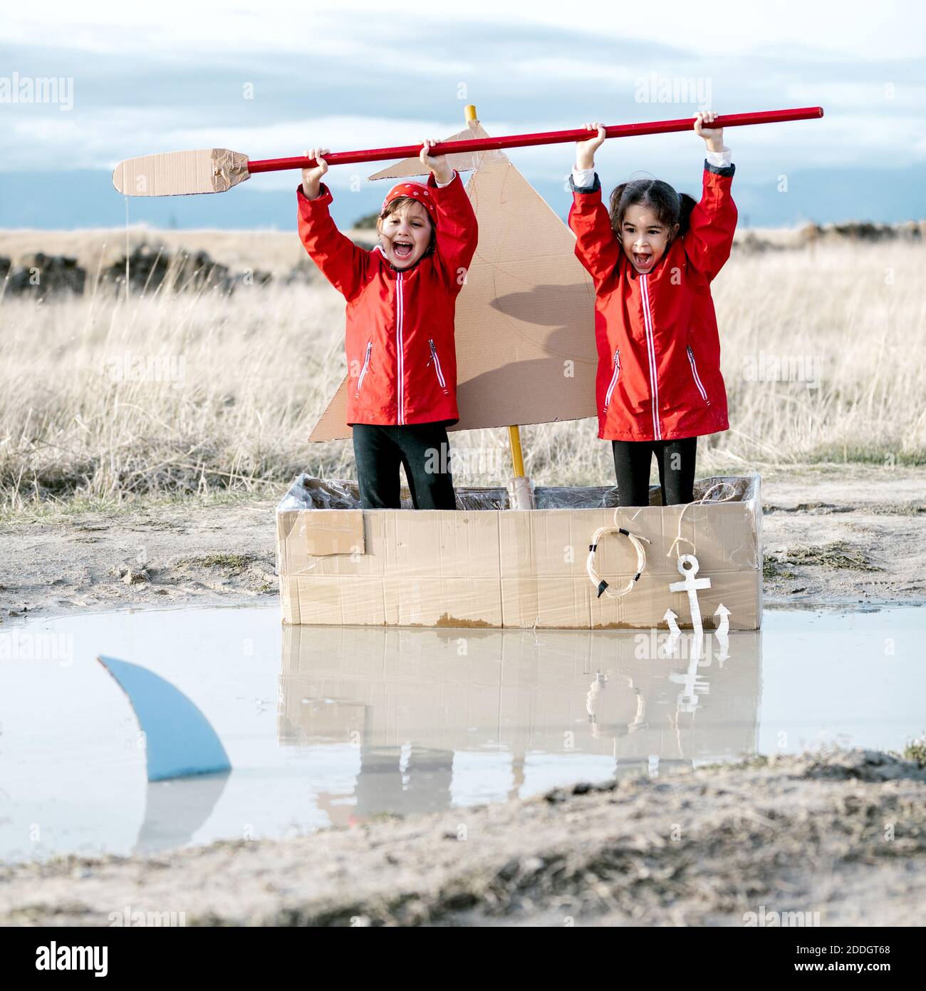 Optimistic children standing in carton boat with paddle above heads ...