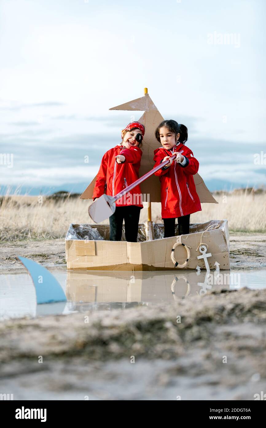 Optimistic children standing in carton boat with paddle above heads ...