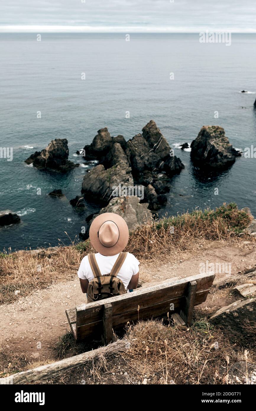 Back view high angle of male explorer in hat sitting on wooden bench ...