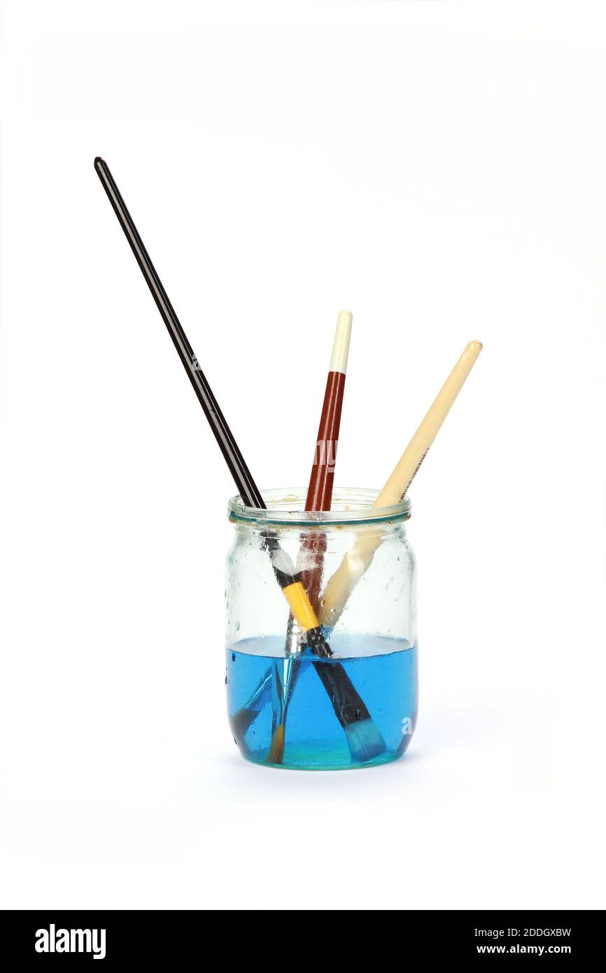 A vertical shot of used paintbrushes in a glass of water isolated on a ...