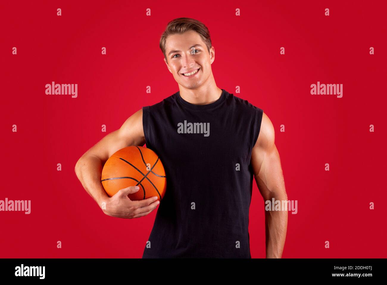 Portrait of happy young basketballer holding ball on red studio ...