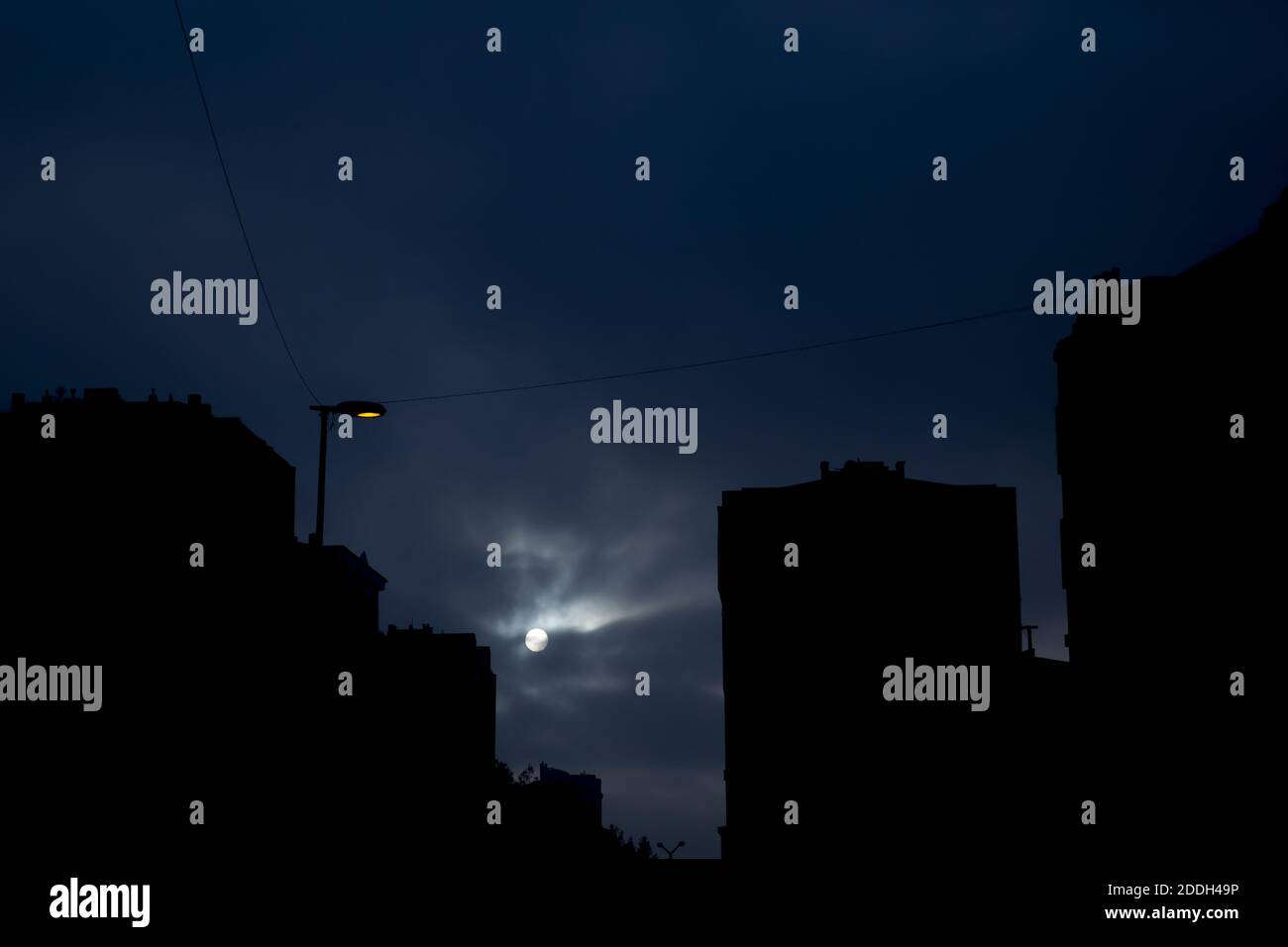 The full moon covered in clouds above residential buildings at night ...