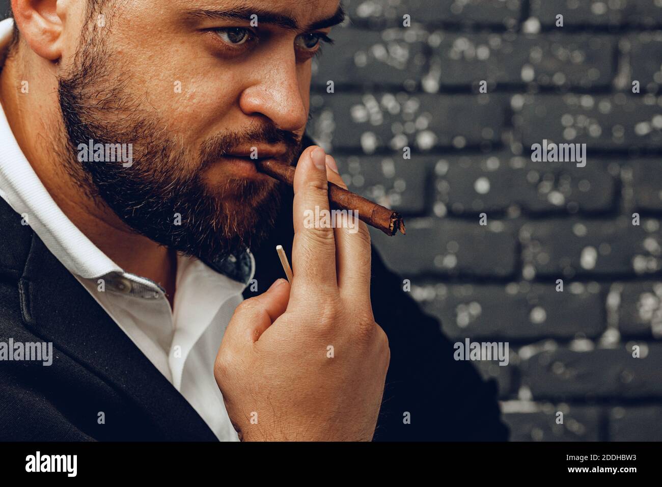 Bearded man smoking cigar against black brick wall Stock Photo - Alamy