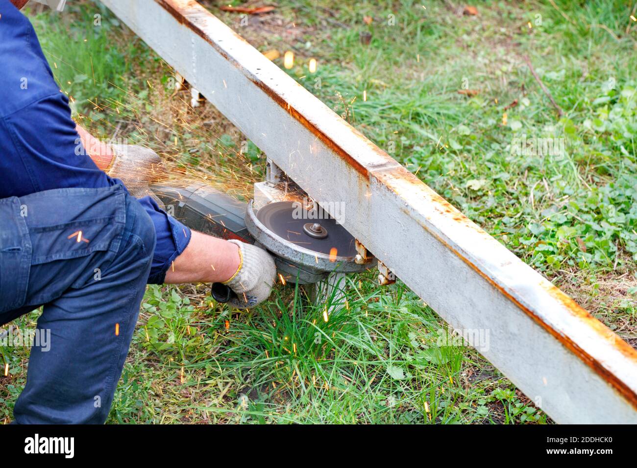 The worker cuts the metal channel with a disc angle grinder with an ...