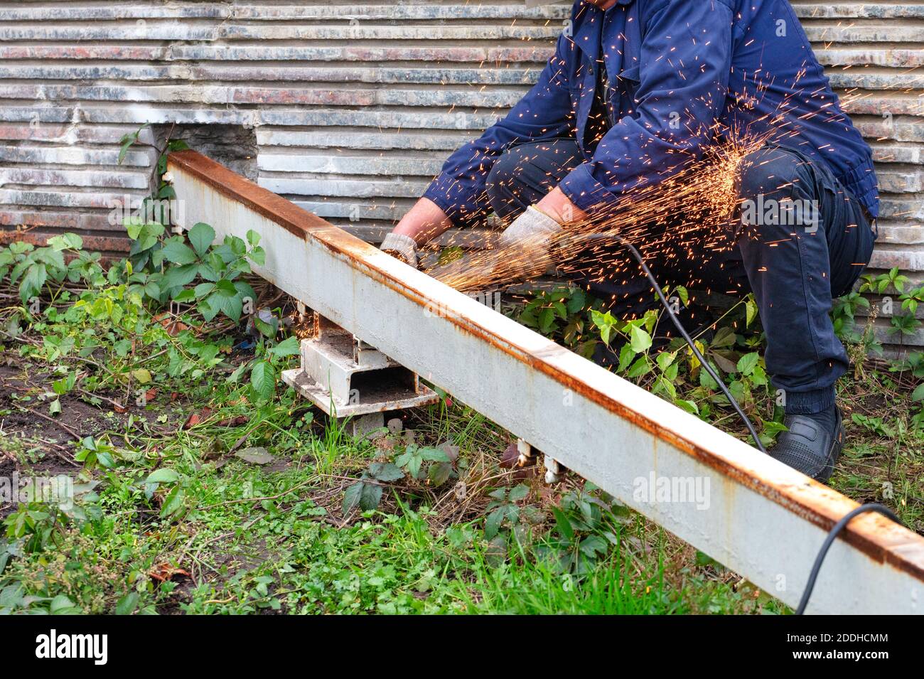 A worker cuts a metal I-beam with an electric disc angle grinder with ...