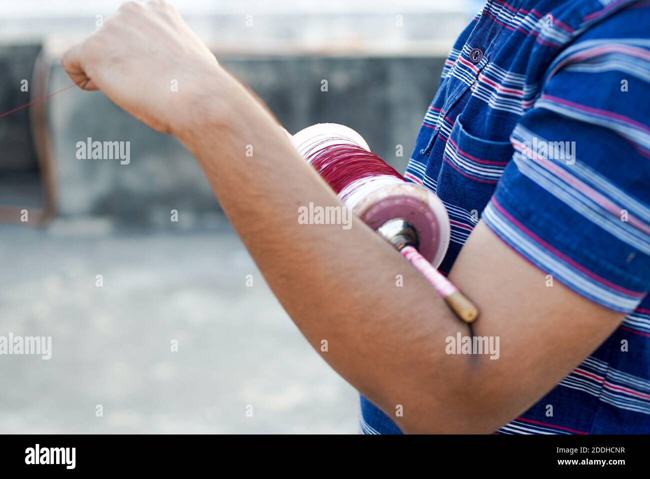 Man holding a charki phirki thread spool in the crook of his elbow and ...