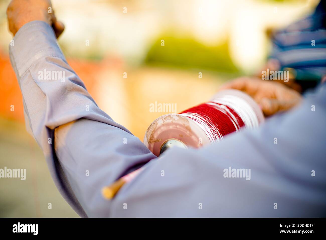 Man holding a charki phirki thread spool in the crook of his elbow and ...