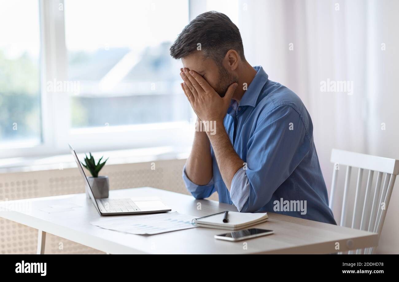 Remote Work Stress. Tired freelancer man sitting at desk at home office ...