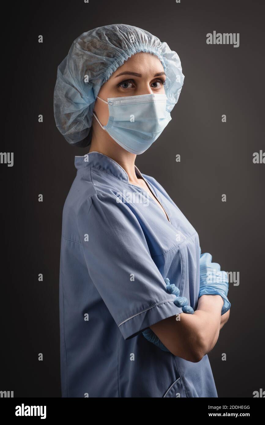 nurse in medical cap and mask standing with crossed arms and looking at ...