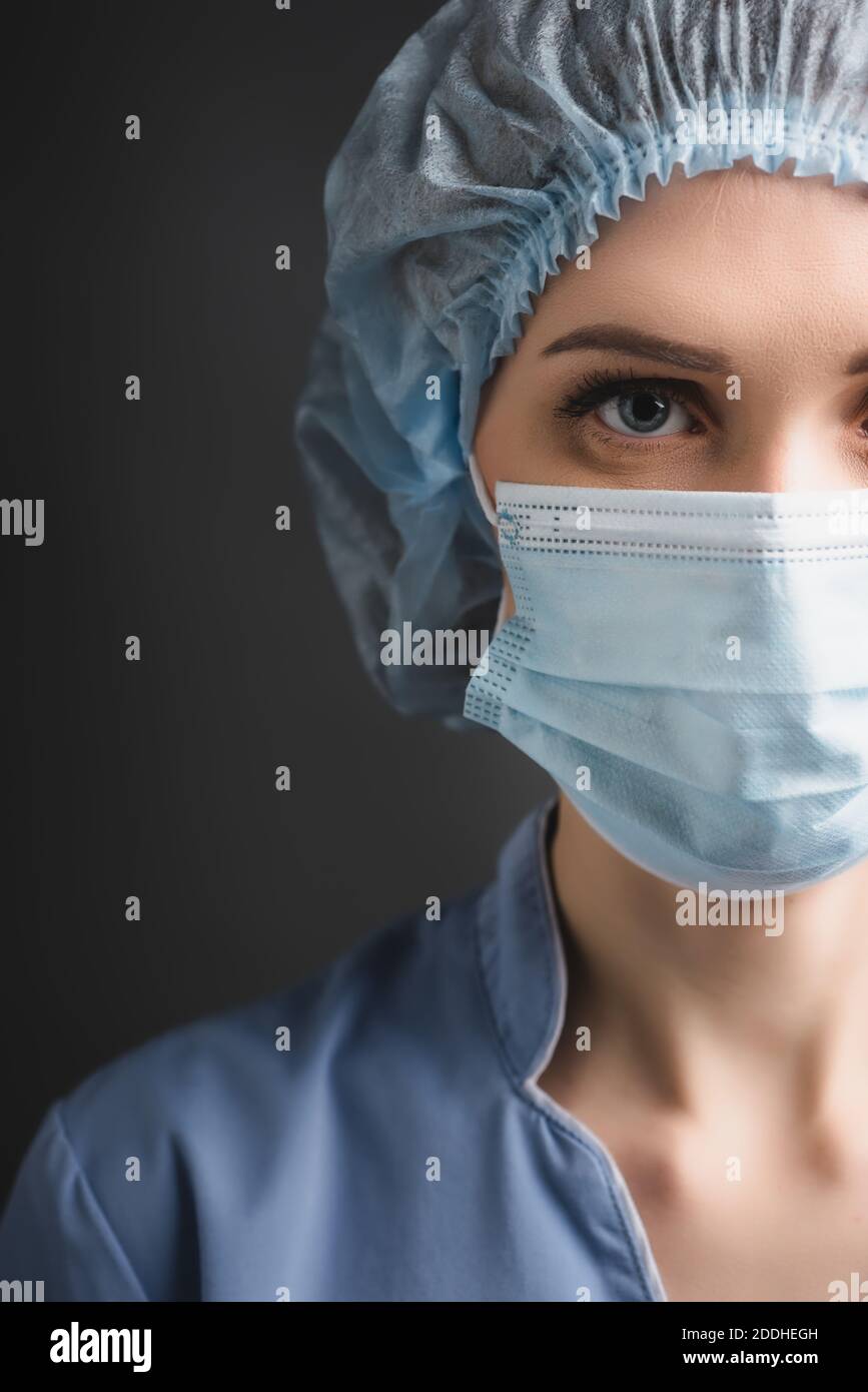 partial view of nurse in medical cap and mask looking at camera ...