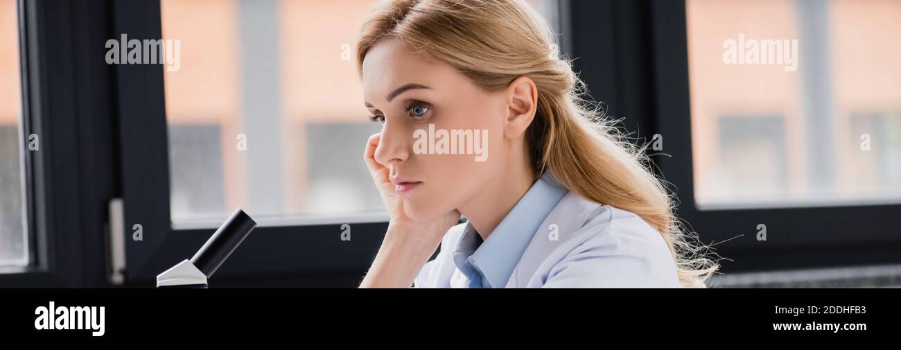 sad scientist leaning on hand near microscope in lab, banner Stock ...