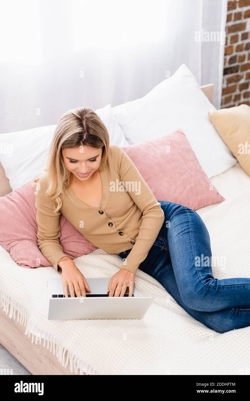 Overhead view of smiling teleworker using laptop while lying on bed ...