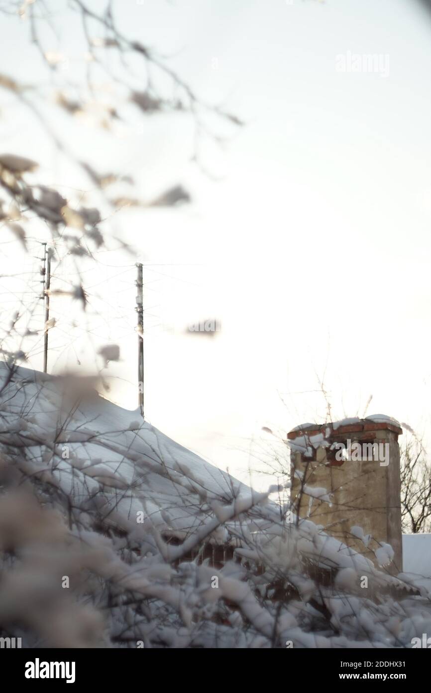Rural chimney and antennas on a snow covered roof and tree branches ...